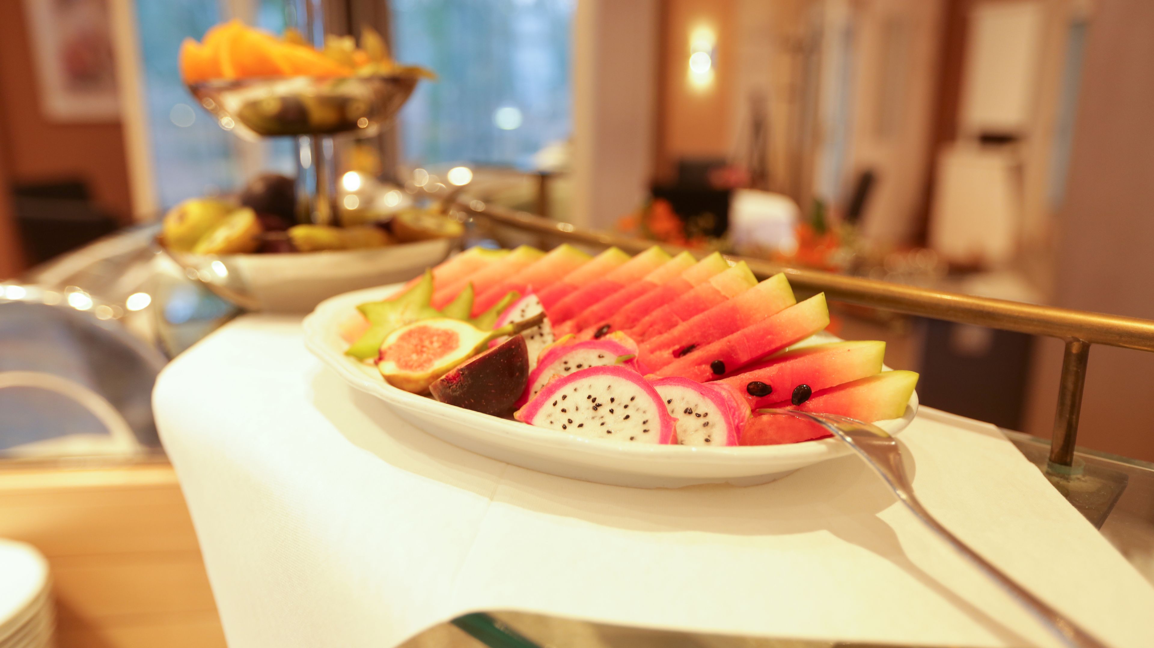 Buffet com diversas frutas e uma tigela de frutas ao fundo.