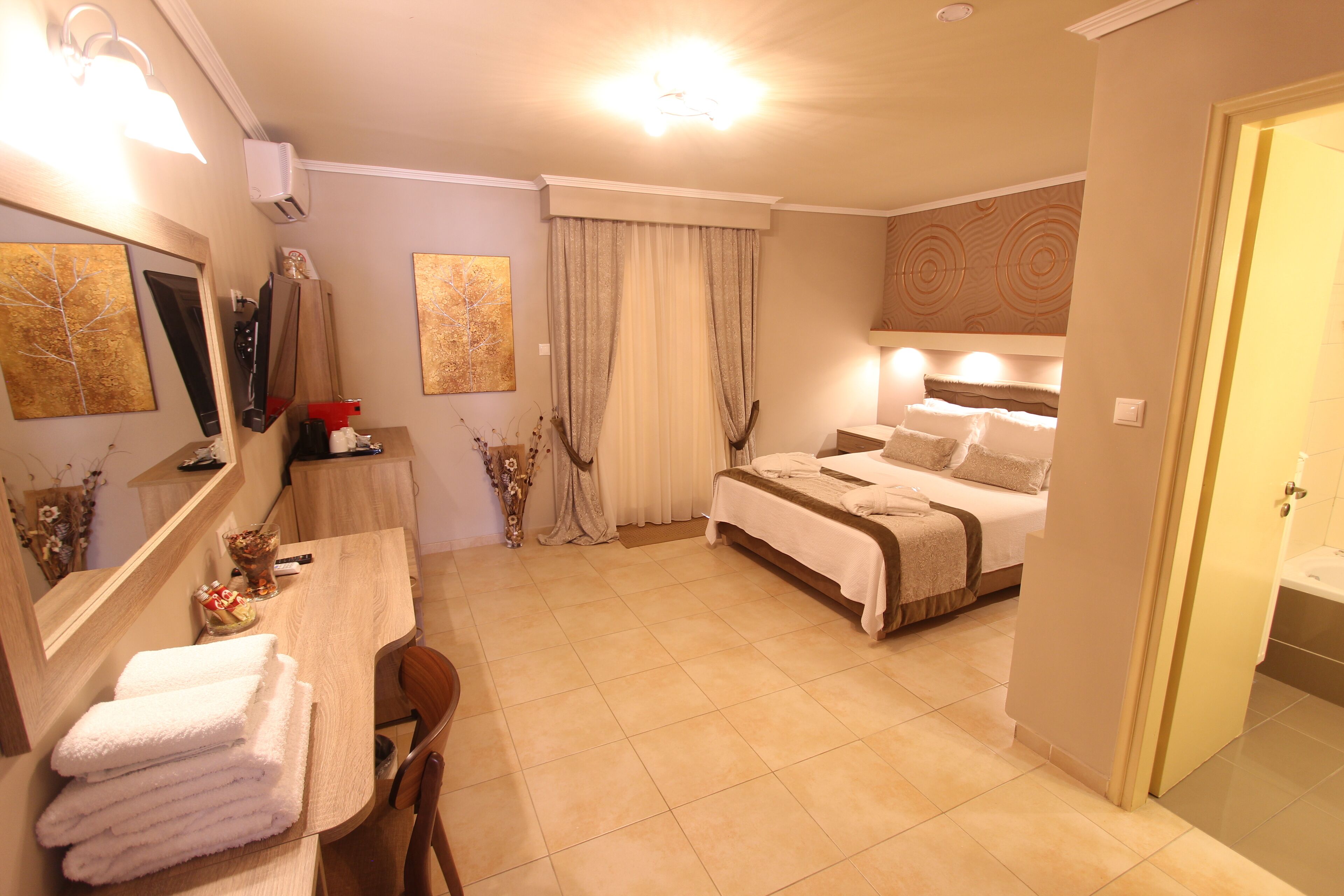 Quarto de hotel com cama, escrivaninha e cadeira, toucador com espelho e banheiro.