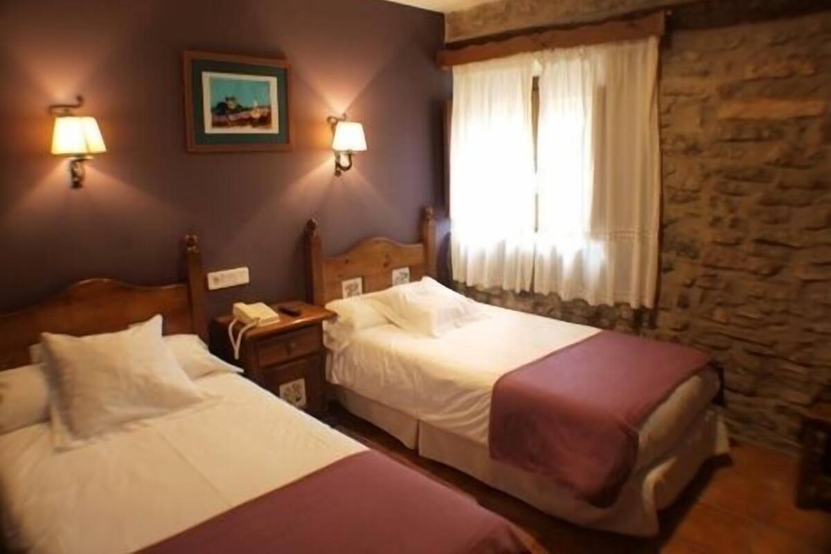Quarto de hotel com duas camas, uma parede de pedra e uma janela com cortinas.