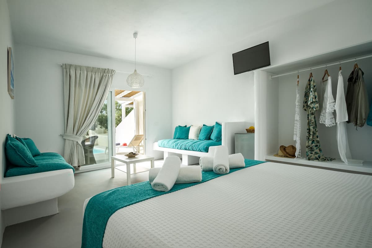 Quarto de hotel moderno com uma cama grande, um sofá, uma mesa pequena e um guarda-roupa.