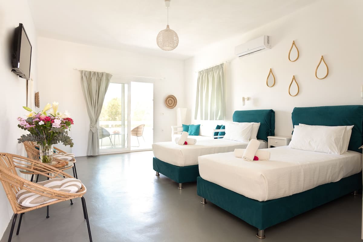 Quarto de hotel com duas camas, televisão, uma janela grande e uma cadeira de vime.