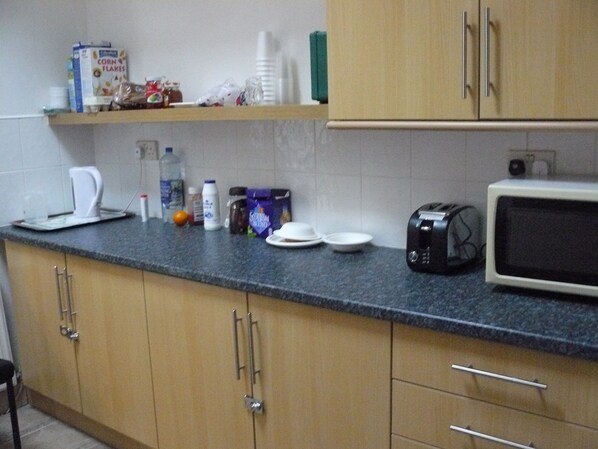 Cozinha com armários de madeira, micro-ondas, torradeira e diversos alimentos sobre o balcão.