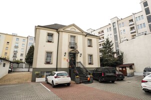 Edifício de vários andares com entrada central, escadaria e estacionamento com diversos carros.