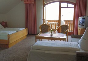 Quarto com duas camas de solteiro, uma mesinha com cadeiras, televisão e varanda com deck de madeira.