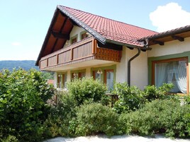 Uma casa de dois andares com varanda, telhado de telhas vermelhas e um jardim frontal.