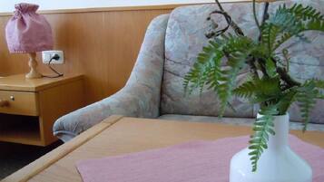 Quarto com mesa de cabeceira de madeira, tecido rosa, vaso branco com planta e sofá estampado com flores.