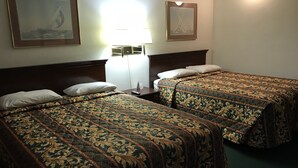 Quarto de hotel com duas camas de solteiro, uma mesinha de cabeceira, uma luminária e duas molduras com fotos na parede.