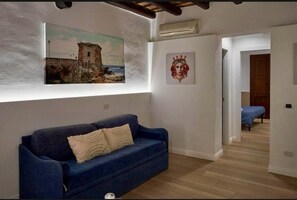 Um quarto com um sofá azul, uma pintura de um castelo e uma obra de arte com coroa na parede.