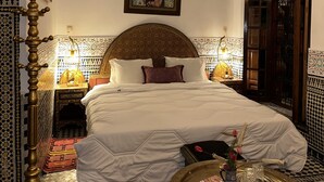 Um quarto tradicional marroquino com uma cama, um enfeite de parede decorativo, um tapete estampado e uma mesinha com bandeja.