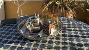 Um terraço com uma mesa estampada, uma bandeja de metal com um bule e copos, e vista para a paisagem urbana.