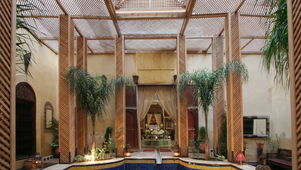 Piscina interior com piso de azulejos, cercada por painéis de madeira e plantas em vasos.