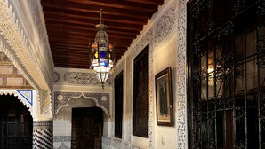 Interior tradicional com trabalhos em azulejos ornamentais, um banco de madeira e um candeeiro suspenso.