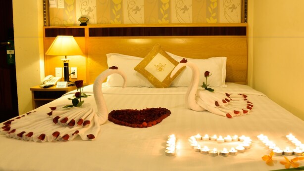 Quarto de hotel com cama bem arrumada, abajur, telefone e arranjos florais decorativos.