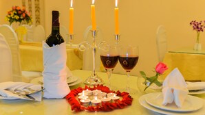 Mesa posta para dois, com velas, copos de vinho, uma garrafa de vinho e uma rosa.