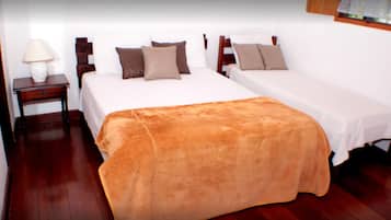 Quarto de hotel com duas camas, uma mesa de cabeceira com abajur e piso de madeira.
