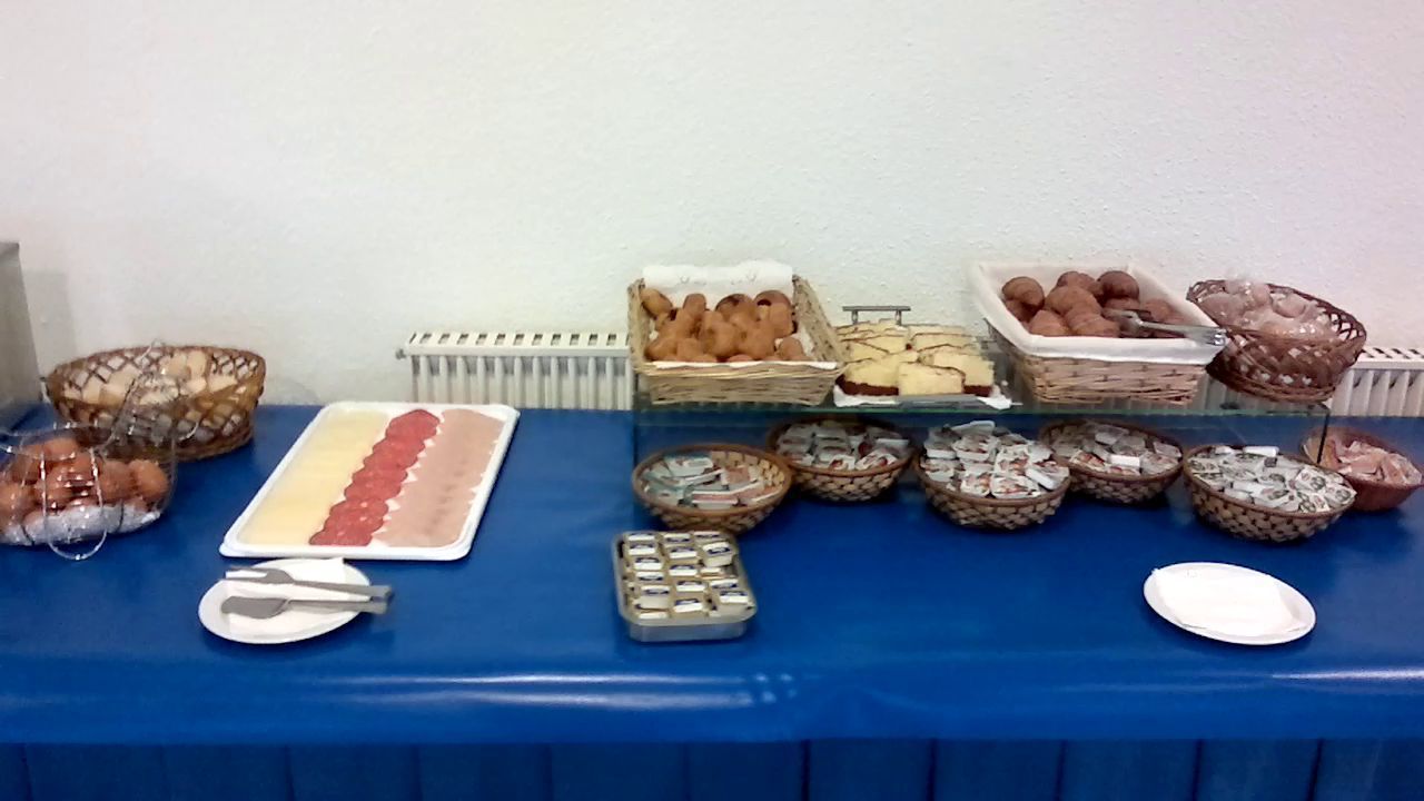 Mesa de buffet com diversos alimentos, incluindo doces e sobremesas, disposta sobre uma toalha azul.