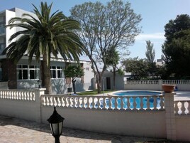 Uma área de piscina com uma cerca decorativa branca, uma palmeira e um edifício com grandes janelas ao fundo.