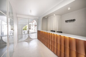 Uma área de recepção de hotel moderna, com um balcão branco, divisória de vidro e vista para a área de estar externa.