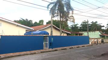 Uma área residencial com uma parede azul, uma casa com telhado vermelho e uma palmeira.