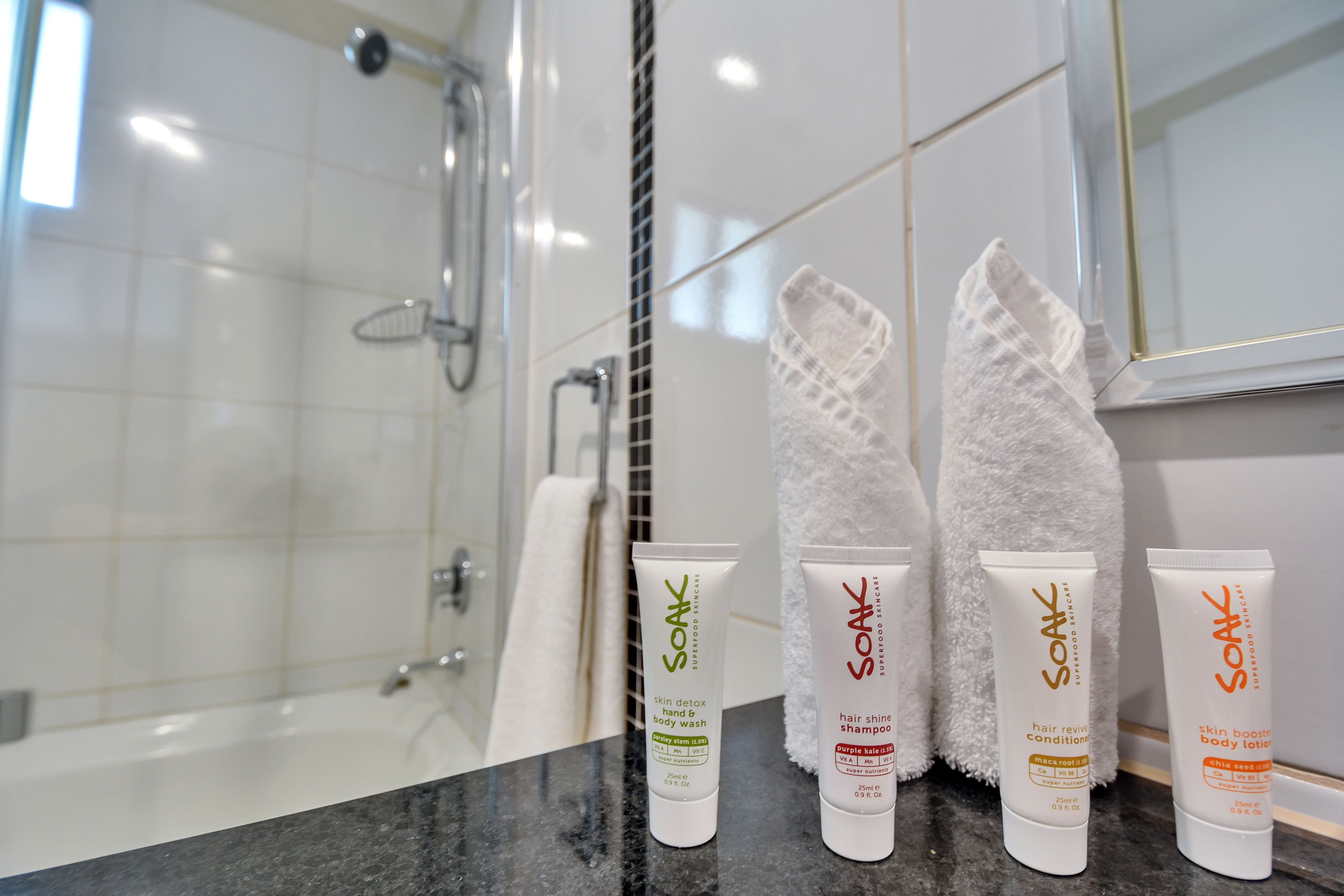 Casa de banho com banheira, chuveiro e três frascos de produtos de cuidados corporais Soak no lavatório.