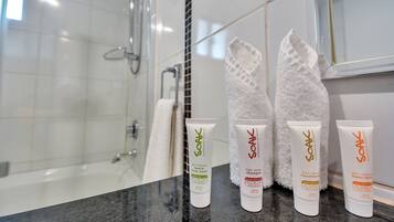 Casa de banho com banheira, chuveiro e três frascos de produtos de cuidados corporais Soak no lavatório.