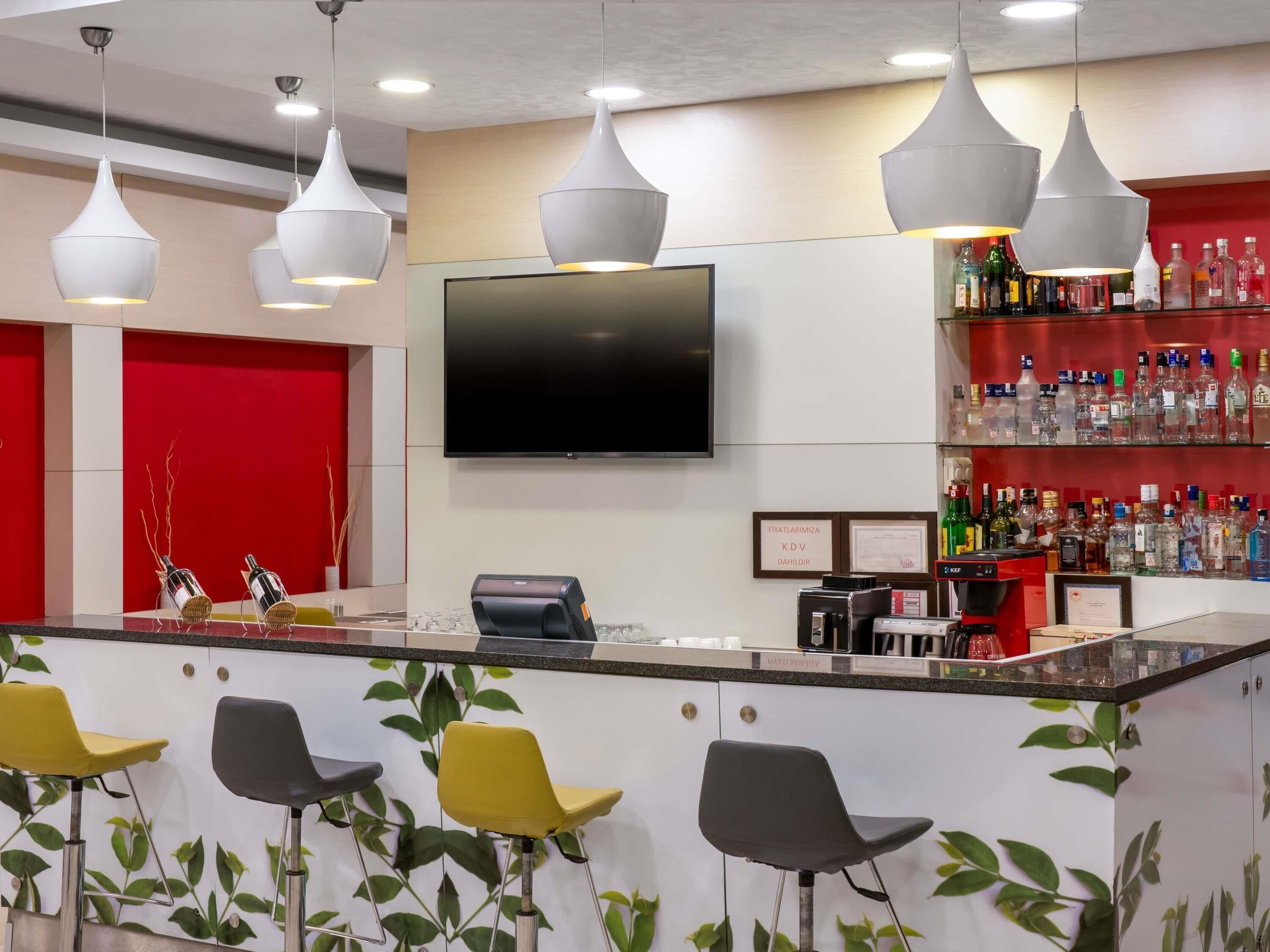 Uma área de bar com televisão de tela plana, várias luminárias pendentes, um balcão e uma variedade de garrafas de bebidas.