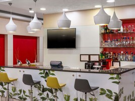 Uma área de bar com televisão de tela plana, várias luminárias pendentes, um balcão e uma variedade de garrafas de bebidas.