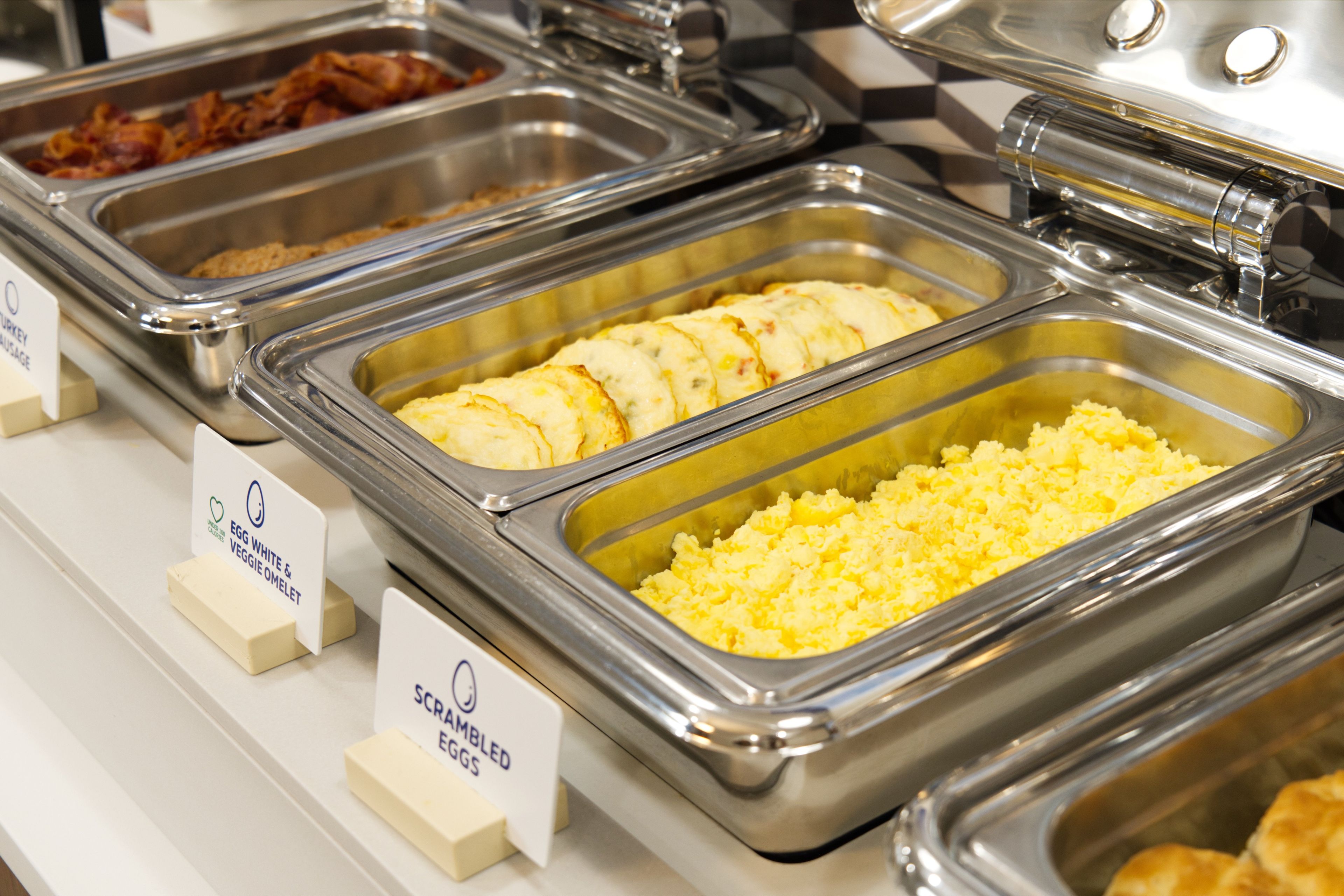 Buffet com recipientes identificados e diversos tipos de comida.