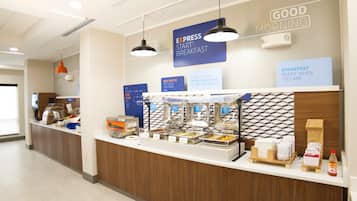 Espaço de buffet de café da manhã com diversas opções de alimentos, um letreiro com 'Bom dia' e uma placa indicando 'Café da manhã pronto quando você estiver'.