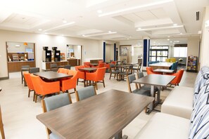 Amplo espaço interno com diversos arranjos de assentos, incluindo mesas e cadeiras, e um balcão possivelmente para serviço de alimentação.