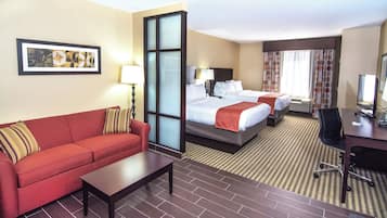 Quarto de hotel com sofá vermelho, cama com duas almofadas, escrivaninha com computador e uma janela grande com cortinas.