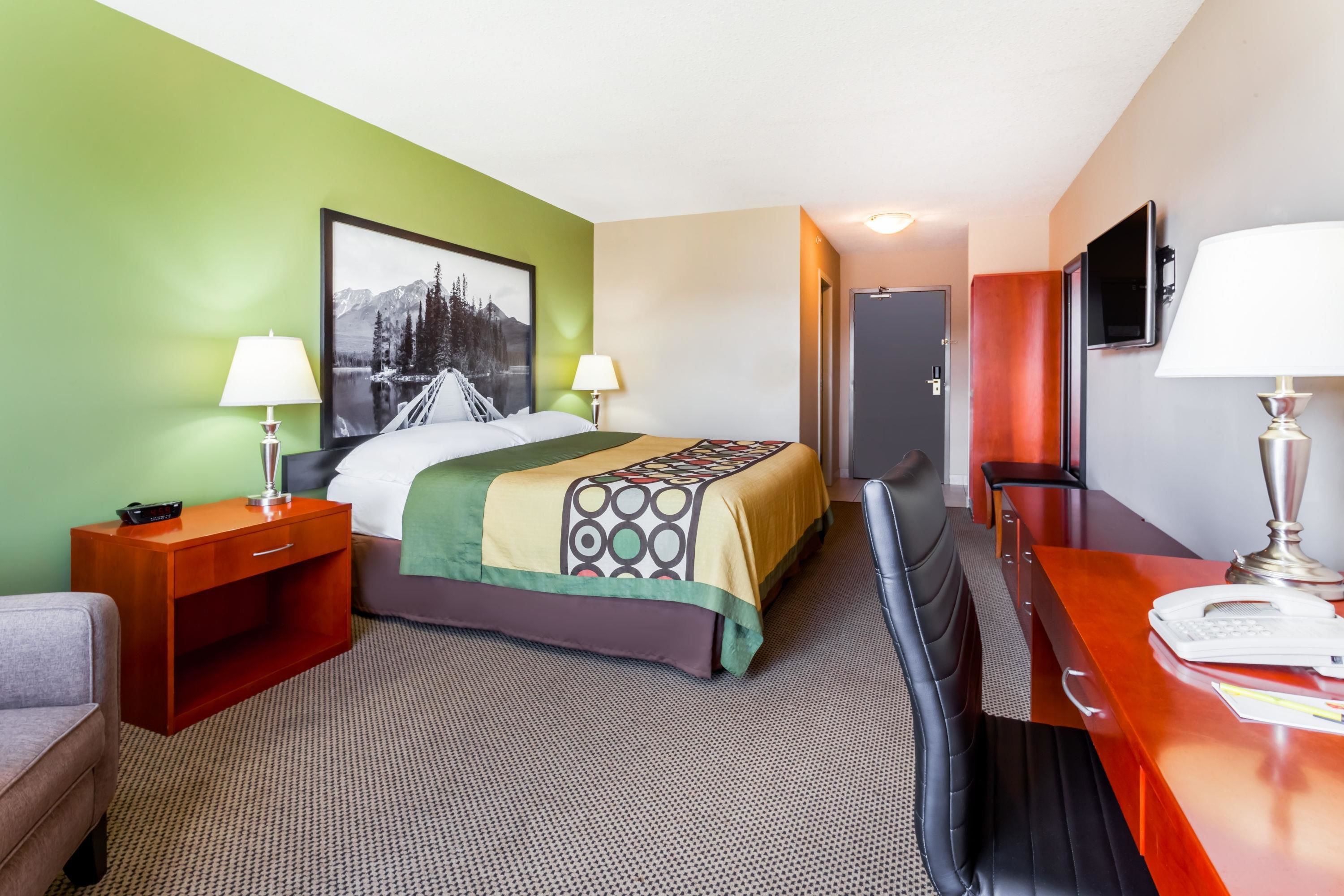 Quarto de hotel com cama, escrivaninha, cadeira, televisão e porta.