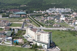 Um hotel com vários andares, piscina e vegetação exuberante ao redor, com outros edifícios nas proximidades.