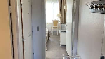 Corredor de hotel com uma cama, uma cadeira e uma mesa.