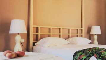 Quarto de hotel com cama, duas luminárias de cabeceira e uma mesa com frutas.