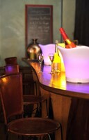 Uma área de bar com uma garrafa de champanhe, copos e um cardápio em lousa ao fundo.