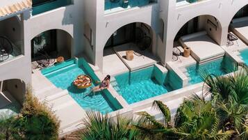 Uma área de piscina com várias seções, incluindo uma piscina central e piscinas menores, cercada por espreguiçadeiras e um espaço para refeições.