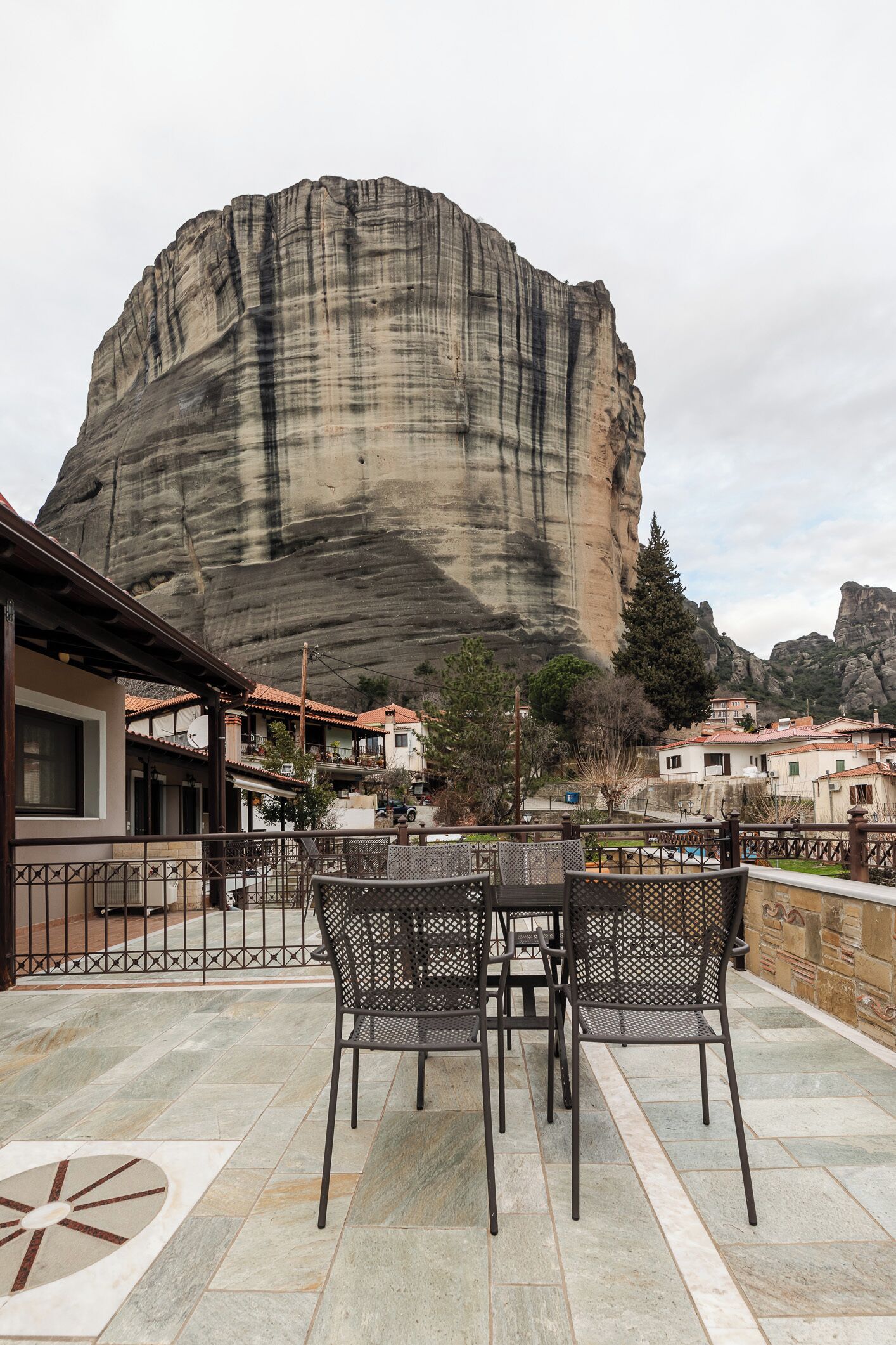 Terraço com mesas ao ar livre, uma grande formação rochosa ao fundo e edifícios residenciais.