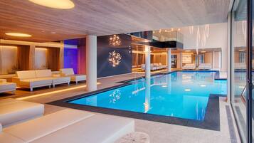 Uma área de piscina interior moderna, com espreguiçadeiras e piscina transparente.