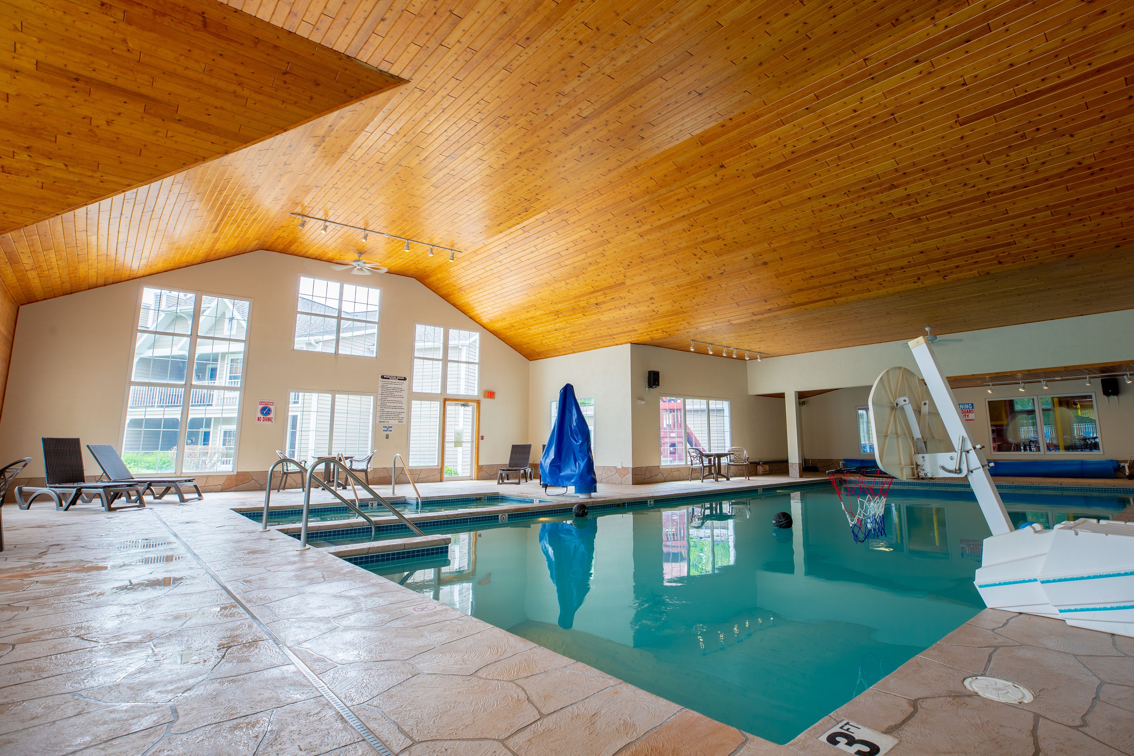 Piscina interior com água cristalina, teto de madeira e chão em azulejos.