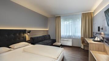 Quarto de hotel com uma cama grande, um sofá, uma mesa de trabalho e uma janela com cortinas.