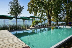 Uma piscina com deck de madeira, cadeiras de descanso e guarda-sóis.