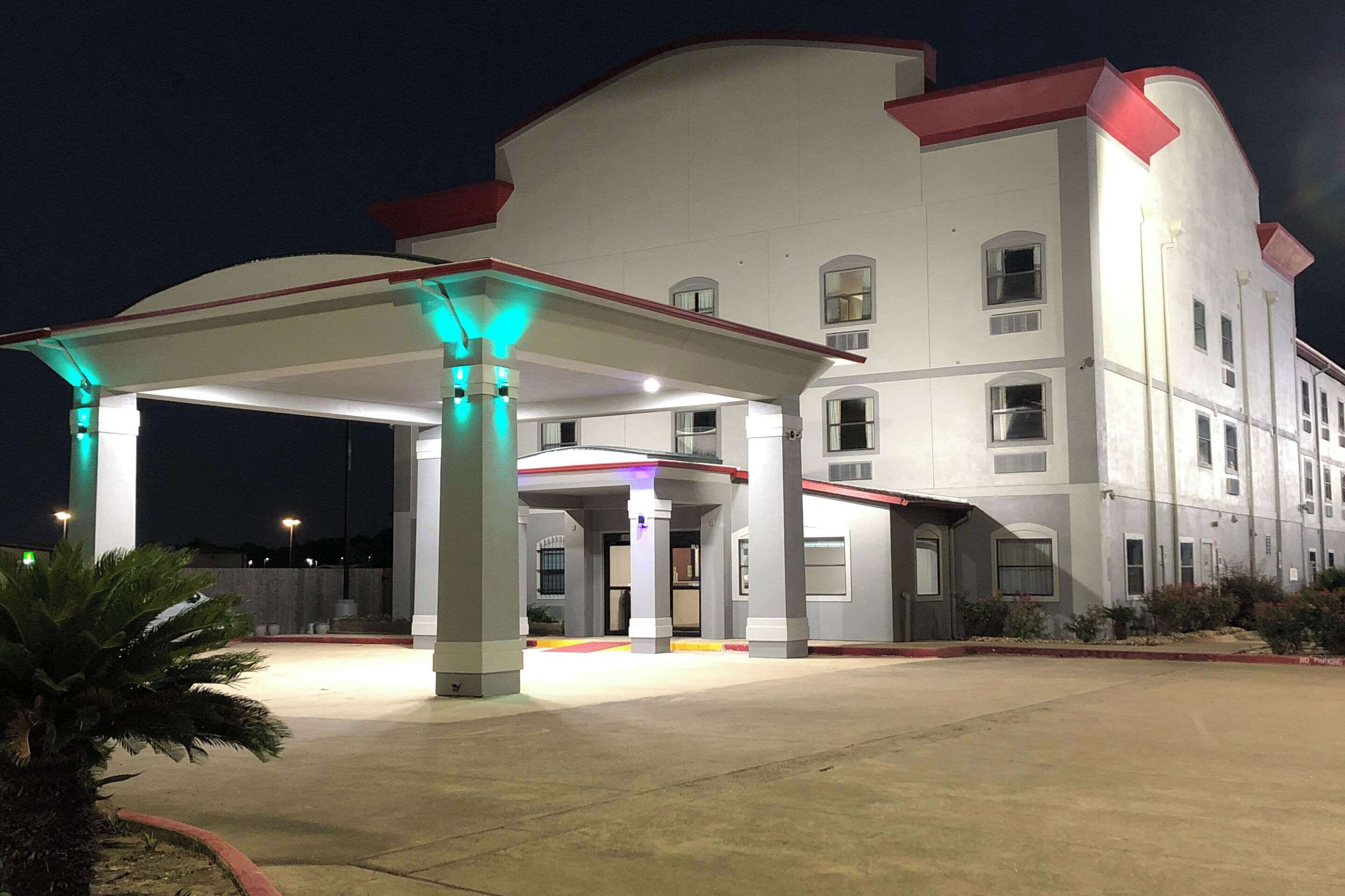 Um edifício de vários andares com área de estacionamento coberta, colunas e uma palmeira.
