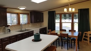 Cozinha moderna com ilha central, área de refeições com mesa e cadeiras, e janelas amplas com cortinas.