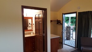 Um corredor leva a um banheiro com pia e secador de cabelo, e uma porta dá para uma varanda com parede de pedra e vista para o verde.