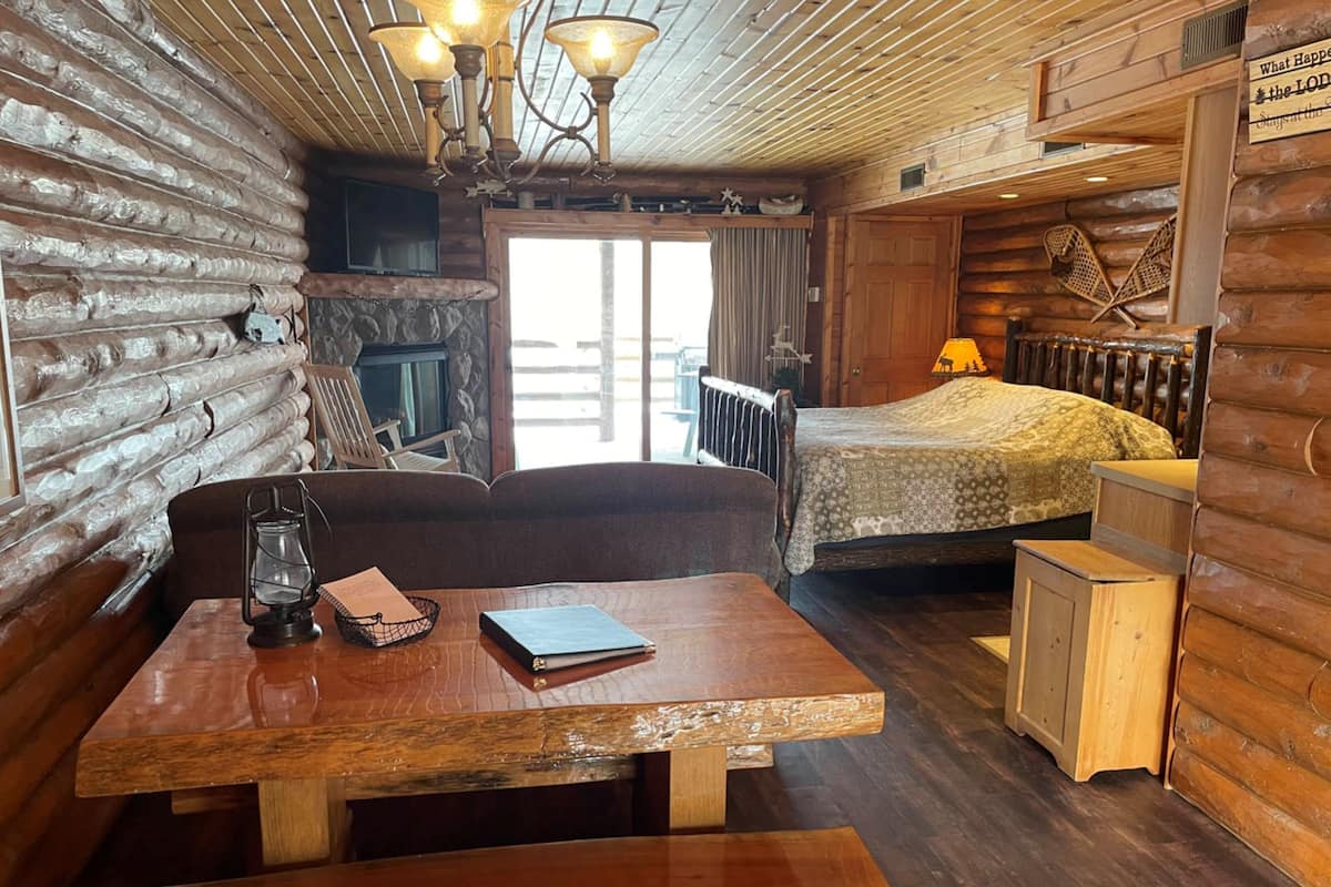 Quarto de cabana de madeira com mesa, banco e cama com colcha estampada.