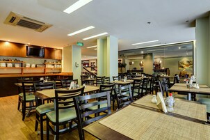 Restaurante com várias mesas e cadeiras, um balcão com televisão e um sinal indicando o caminho para o banheiro.