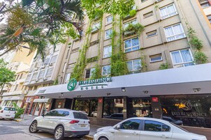 Um hotel com fachada moderna, várias janelas e vegetação na parte externa.
