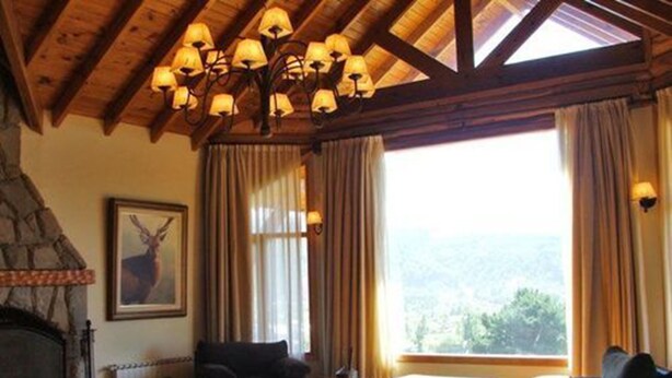 Uma sala de estar aconchegante com lareira de pedra, um candelabro e uma janela ampla com vista para o exterior.