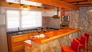 Cozinha com ilha de pedra, balcão de madeira e cadeiras vermelhas.